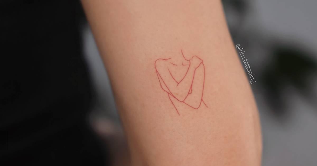 Self hug tattoo in red ink located on the tricep, fine