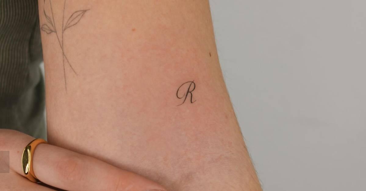 Tiny letter "R" tattoo located on the bicep.