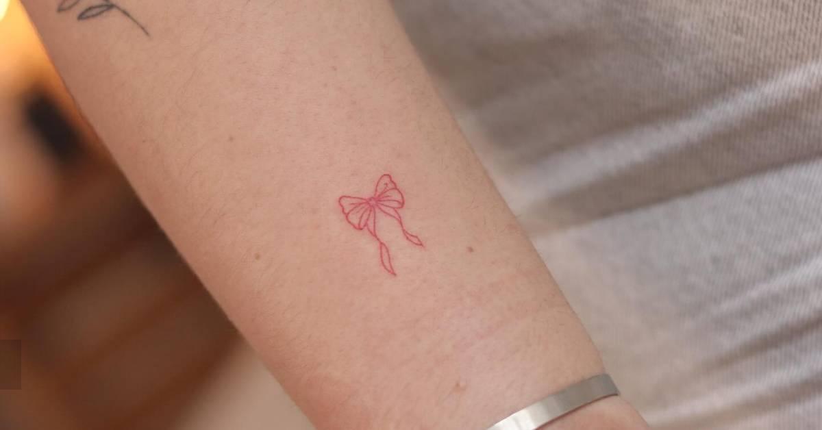 Fine line style red ribbon tattoo located on the wrist.
