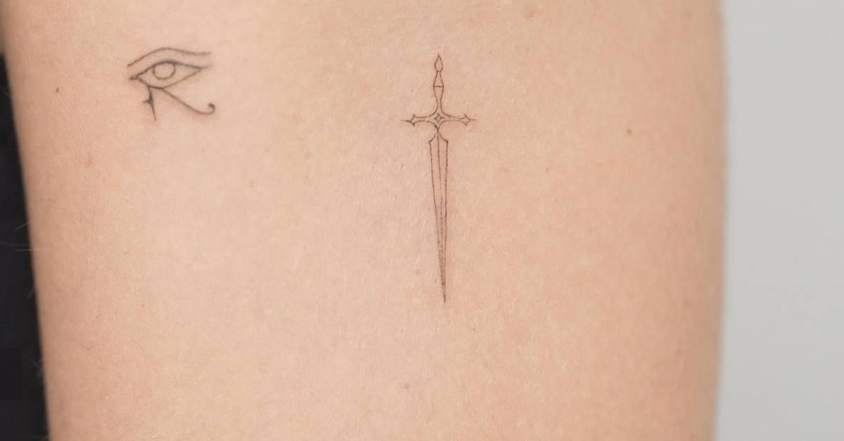 Fine line style dagger tattoo located on the upper arm.