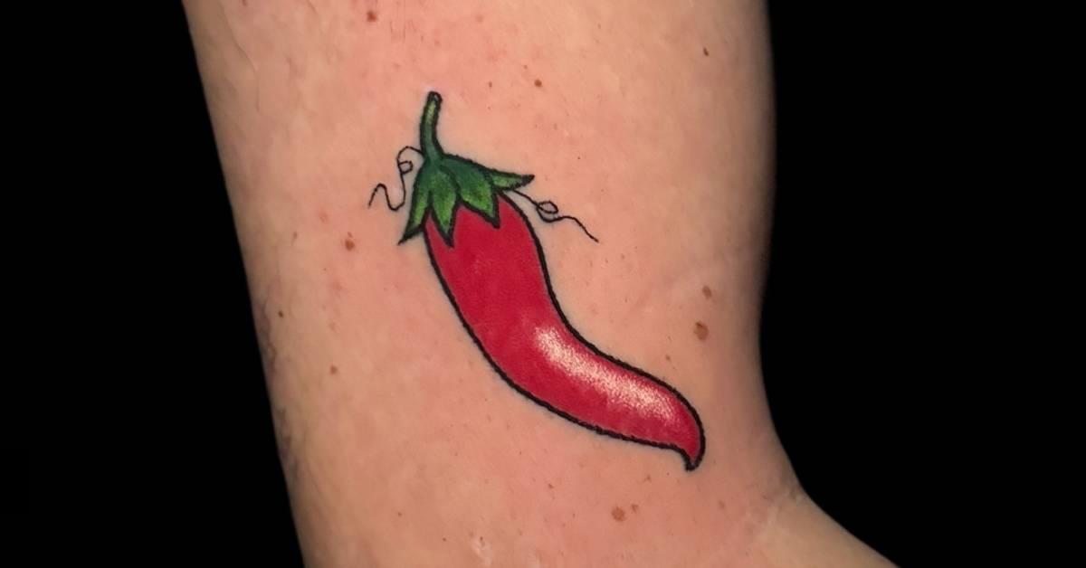 Red chilli pepper tattoo hand poked on the upper arm.
