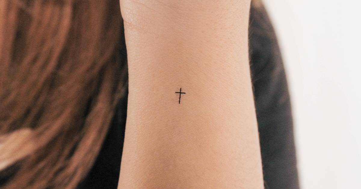 Tiny minimalist cross temporary tattoo located on the