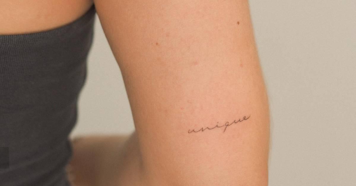 Tattoo of the word "unique" handwritten on the tricep.