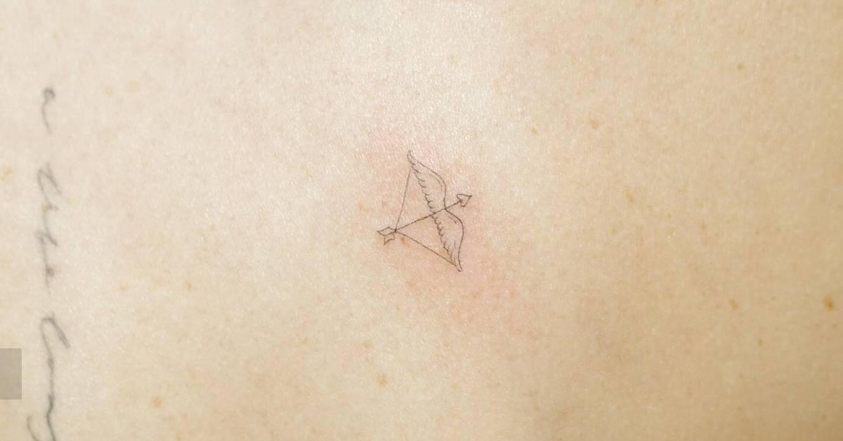 Fine line style wing bow and arrow tattoo located on