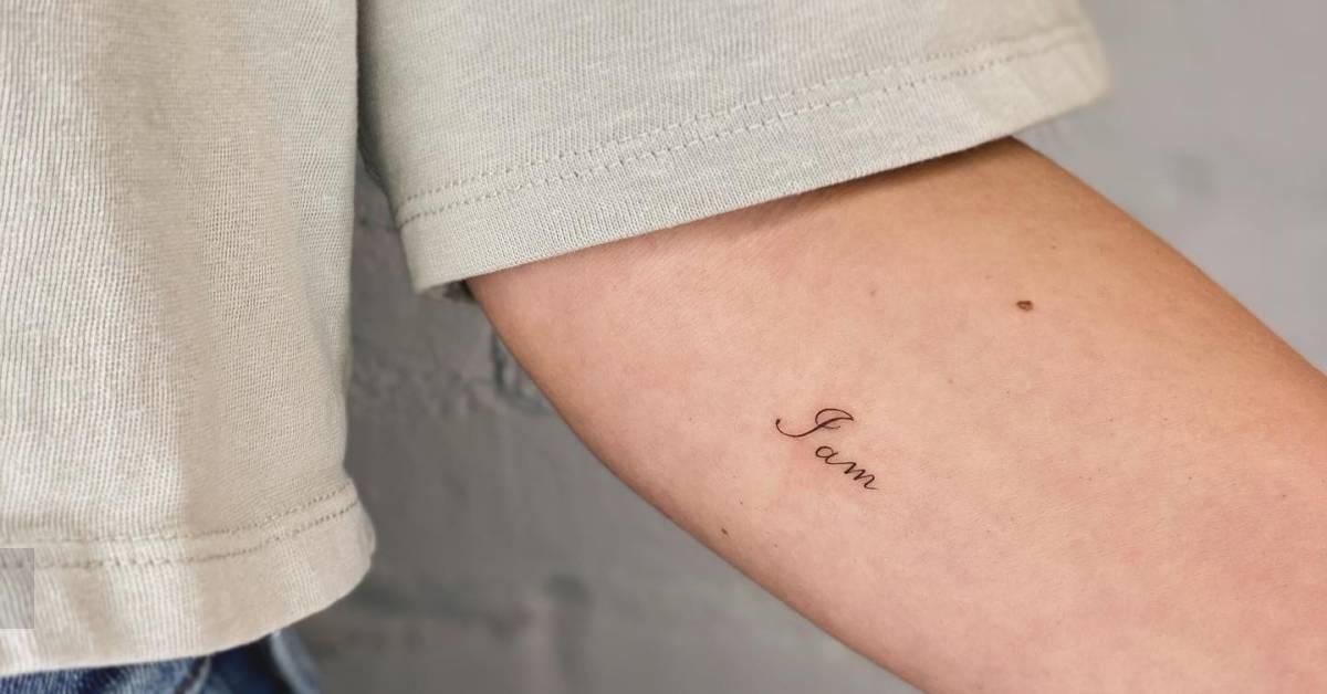 "I am" lettering tattoo located on the inner forearm.