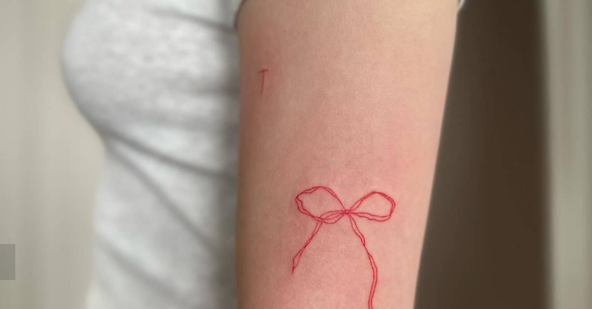Fine line style red bow tattoo located on the upper