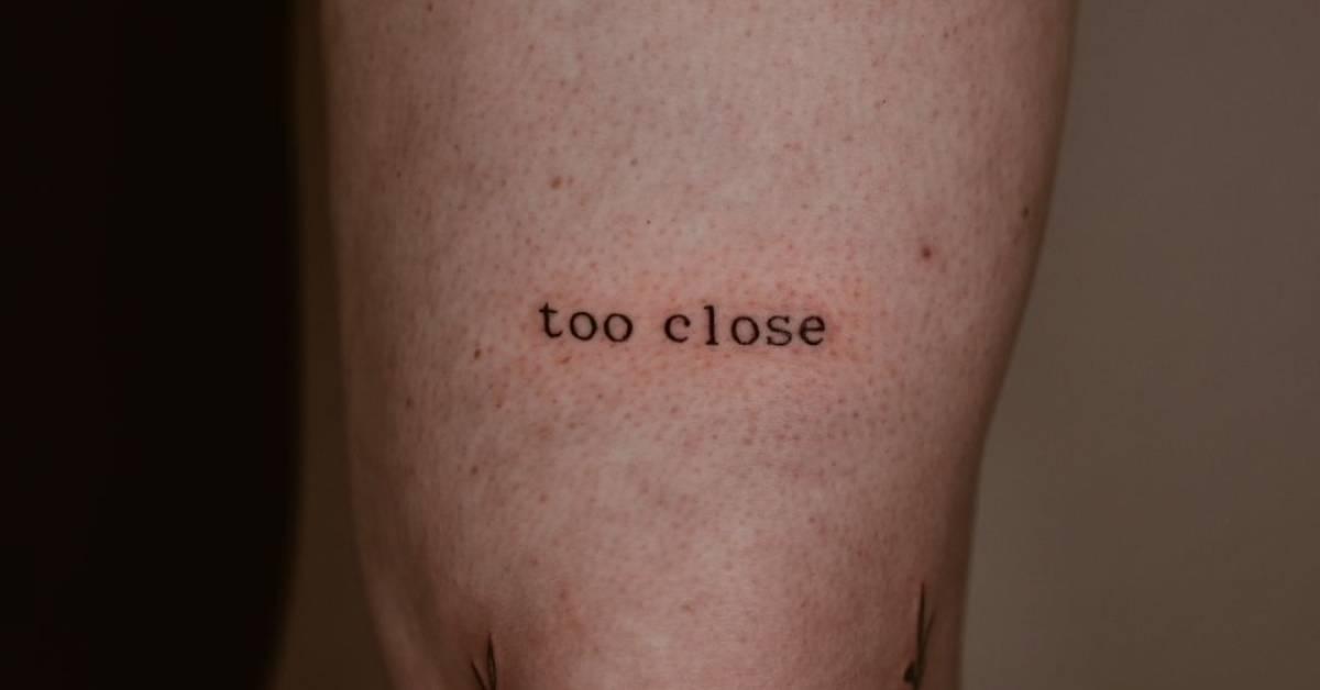 "Too close" lettering tattoo located on the thigh.