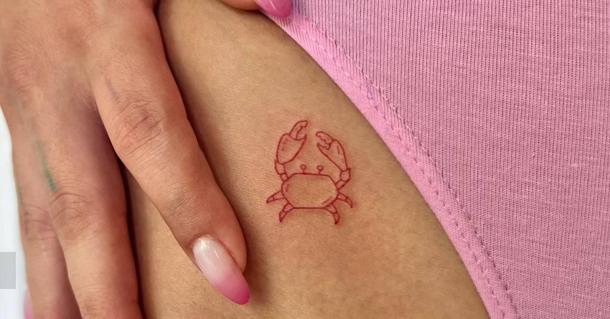 Red crab tattoo located on the pelvis, fine line style.