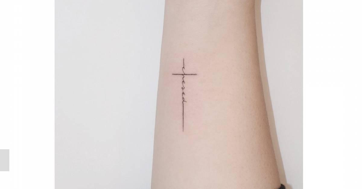 Lettering cross tattoo located on the wrist.