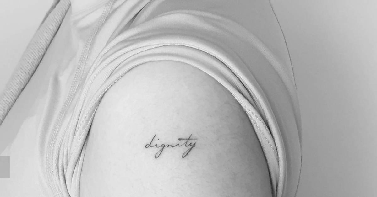 Word "dignity" tattoo handwritten on the shoulder.