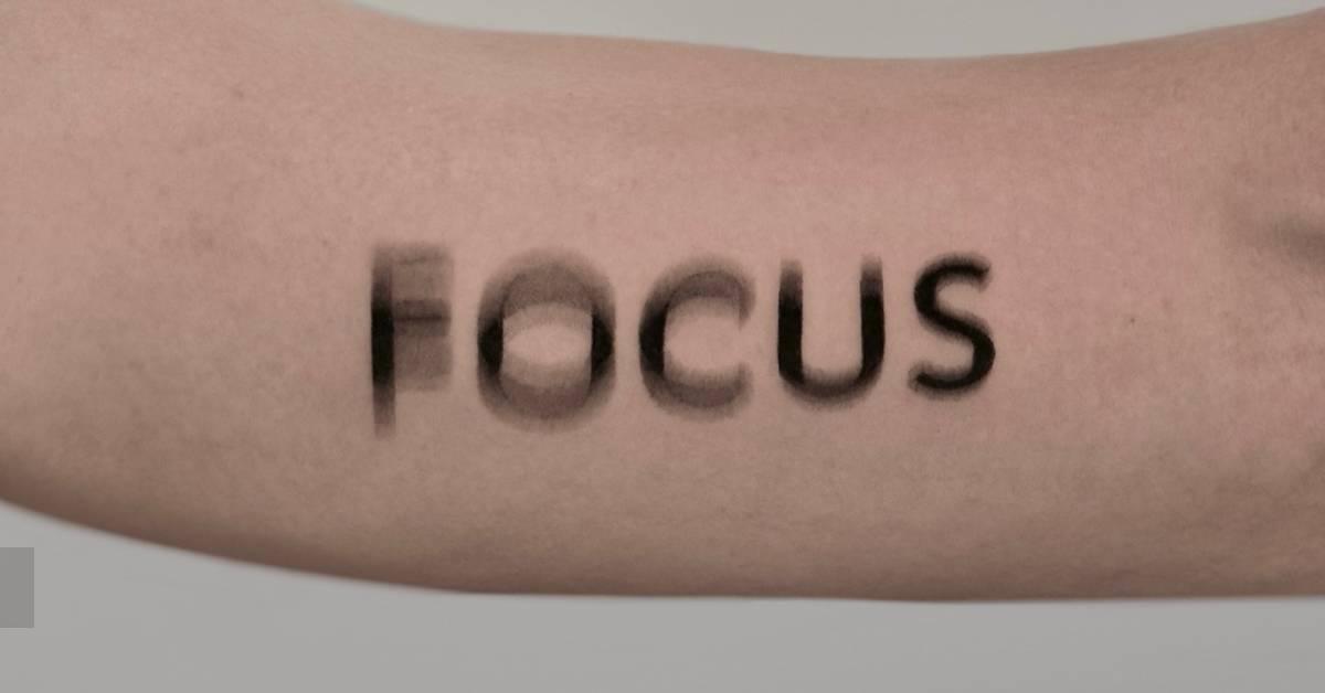 Blurry lettering tattoo of the word "focus" located on