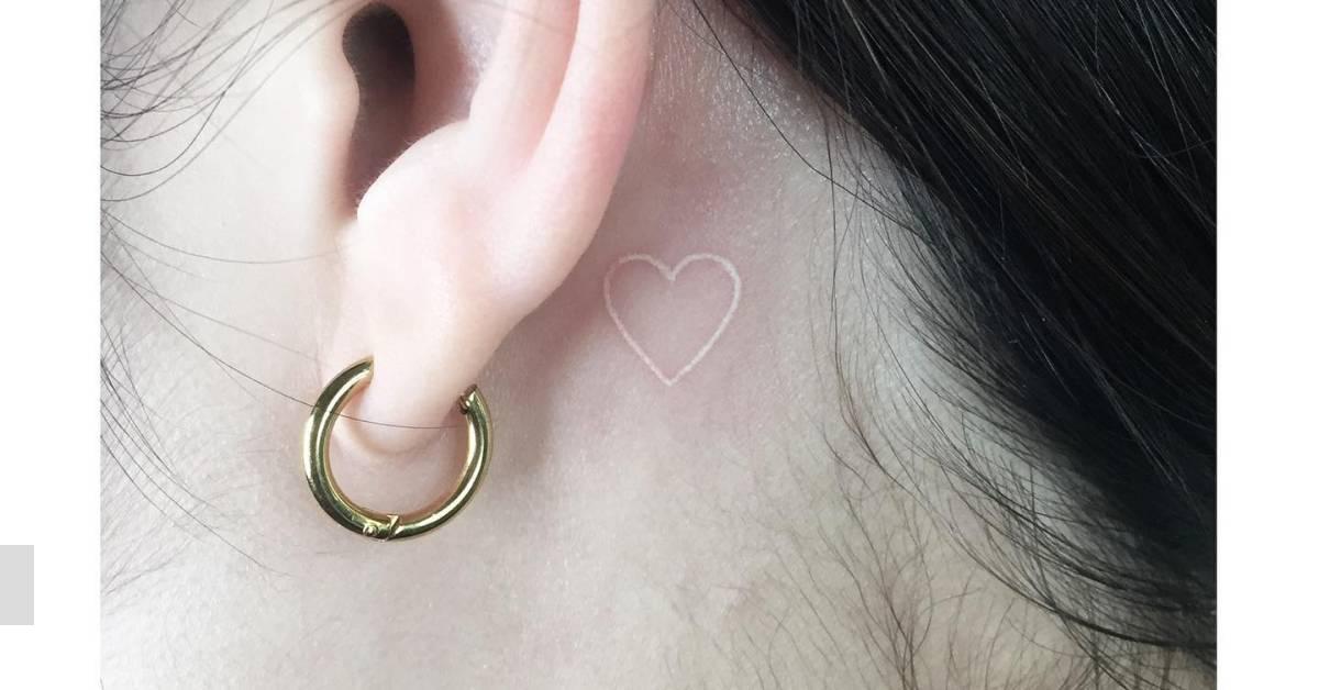 Tiny minimalistic white heart tattoo located behind the