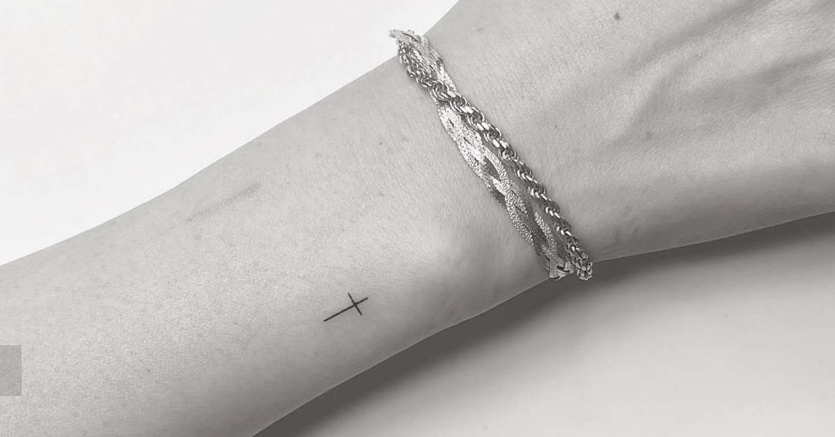 Minimalistic micro cross tattoo located on the wrist.