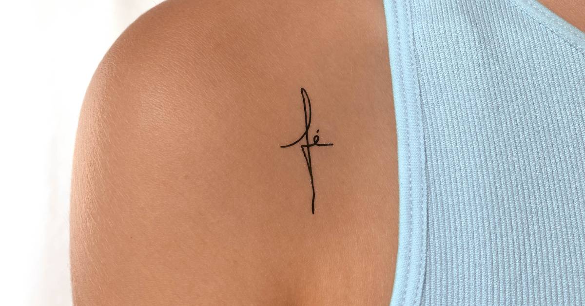 Small "fé" cross temporary lettering tattoo located on