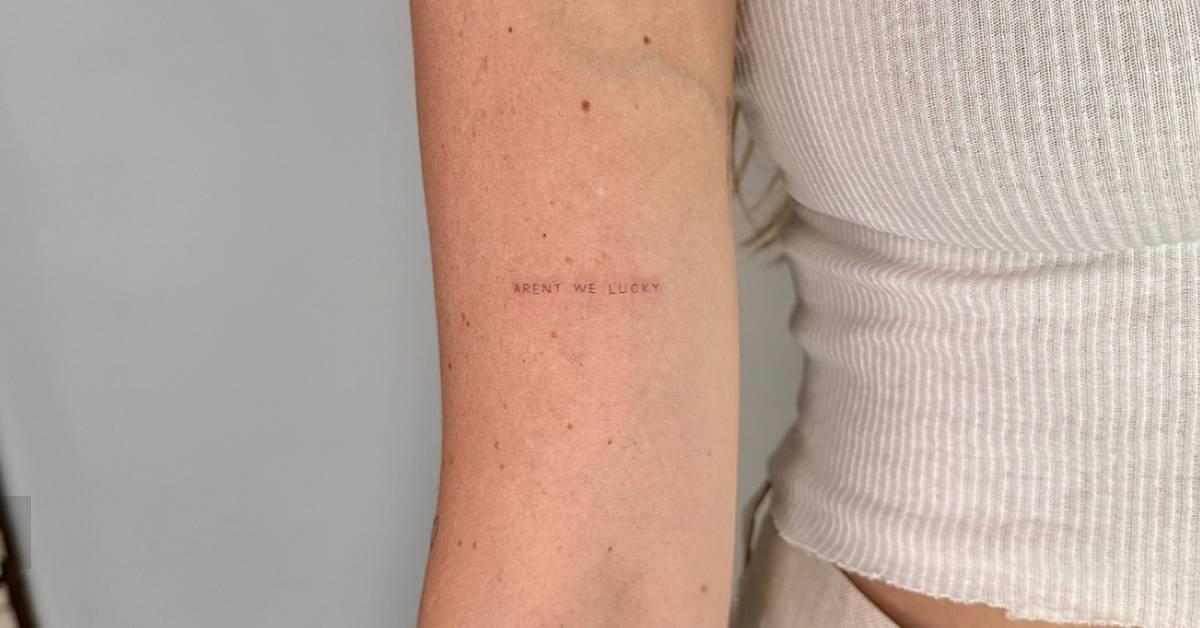 "Aren't we lucky" lettering tattoo placed on the bicep.