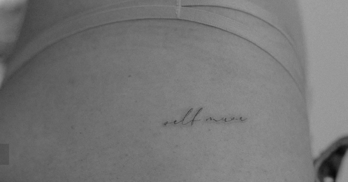 Handwritten 'self muse' tattooed on the hip.