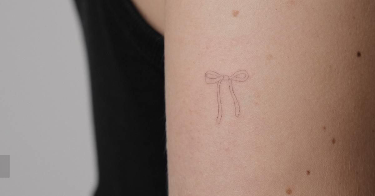 Fine line bow tattoo located on the upper arm,