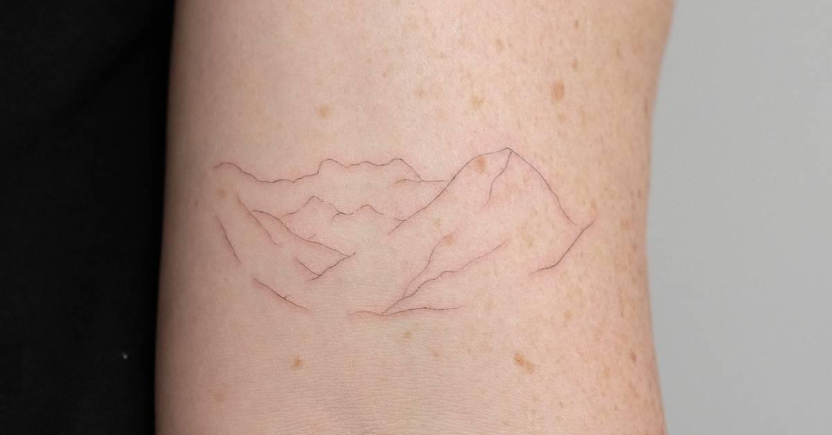 Mountain tattoo located on the bicep, fine line style.