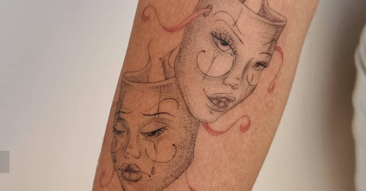 Drama masks tattoo located on the inner forearm,