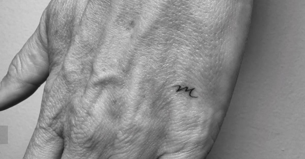 Tiny letter "M" tattoo located on the hand.