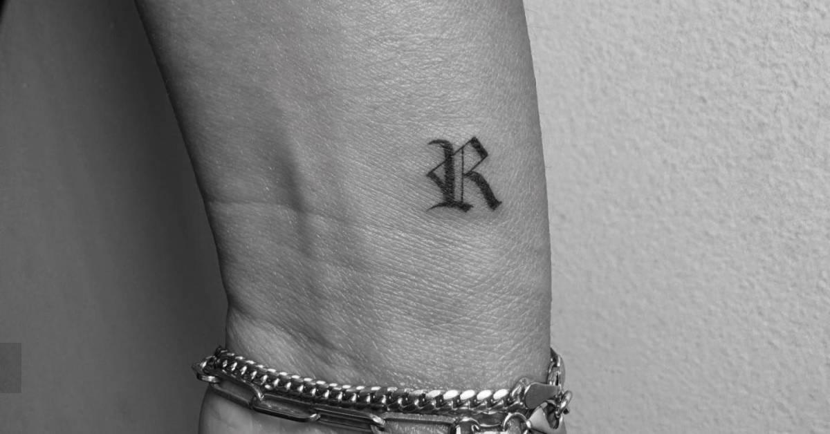 Letter "R" in gothic font tattooed on the wrist.