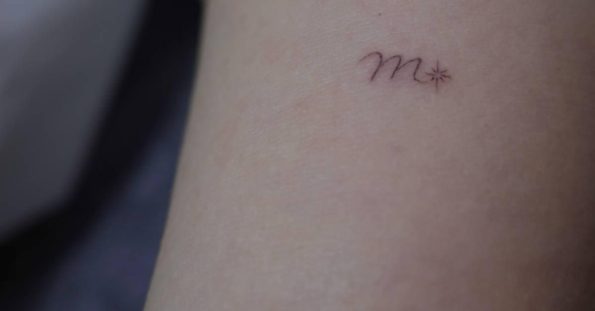 Handwritten minimalistic letter "M" tattoo located on