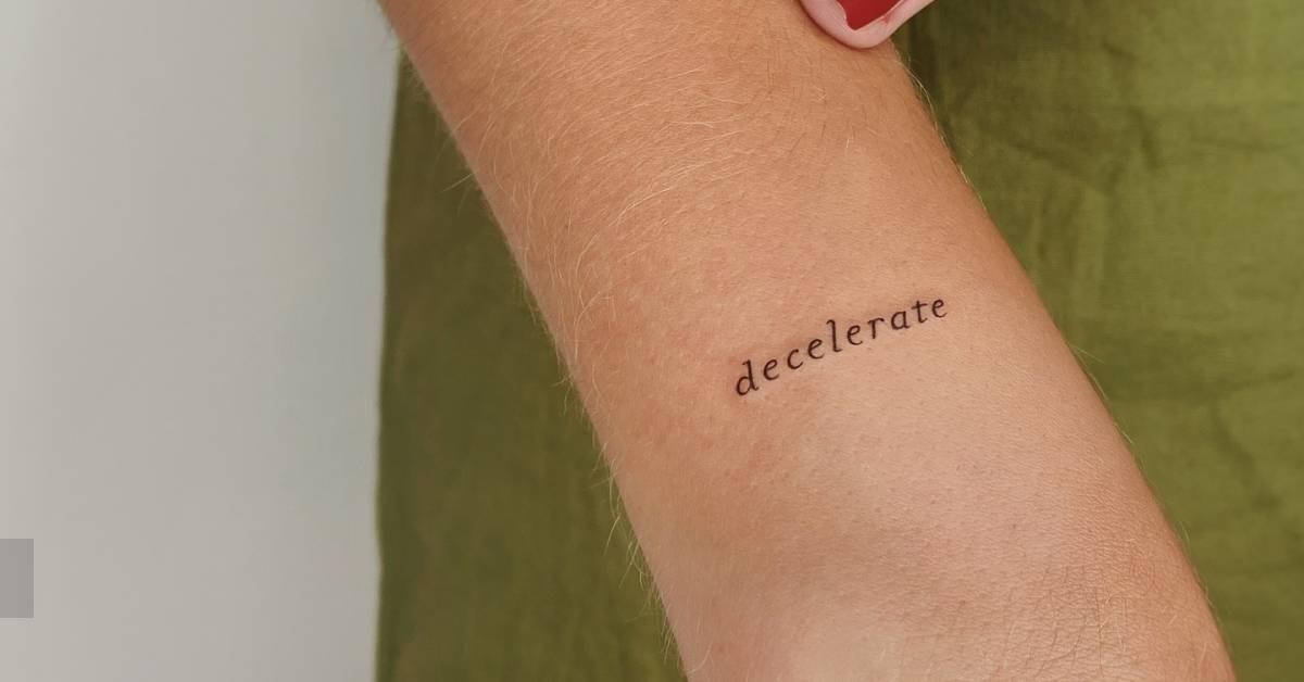 "Decelerate" lettering tattoo located on the wrist.