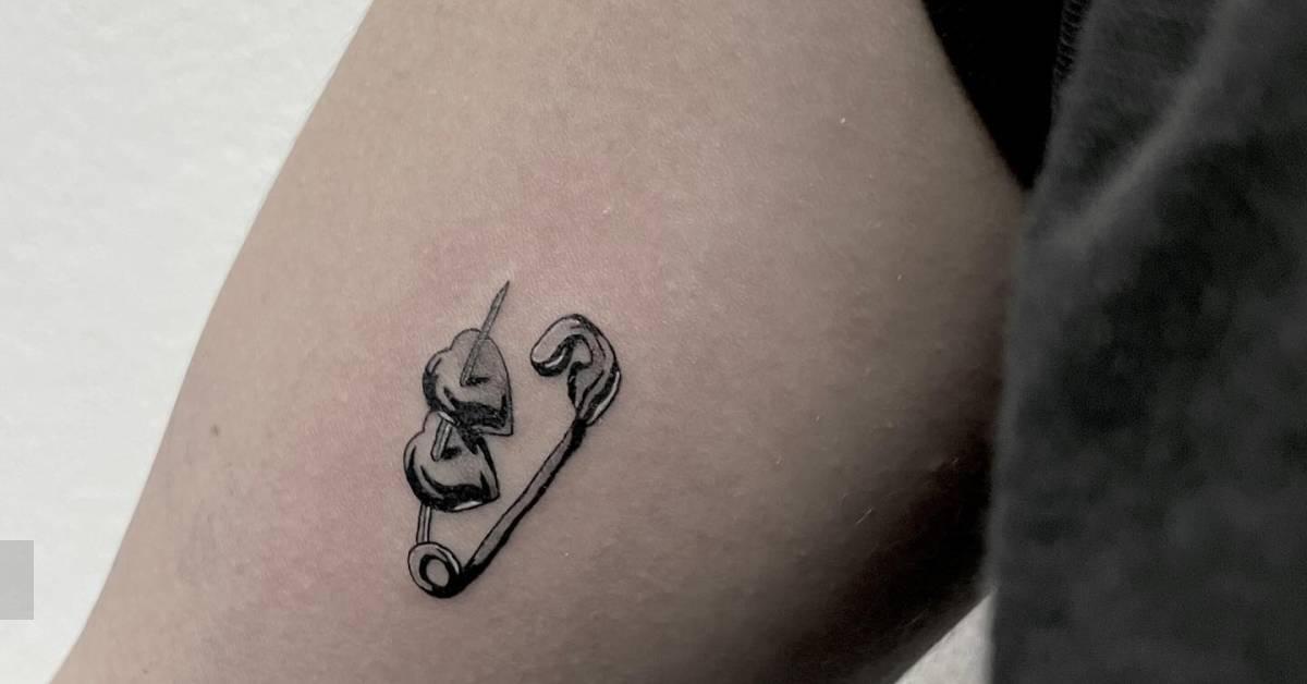 Safety pin and hearts tattoo located on the inner arm.