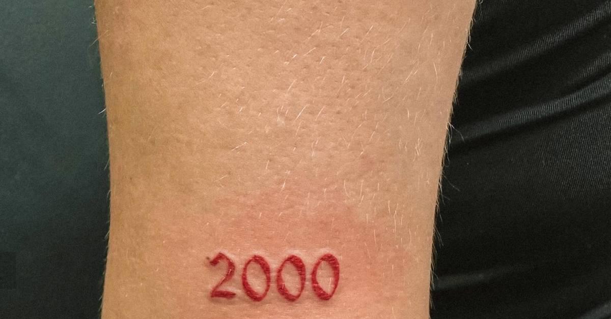 Birth year "2000" in gothic ink tattooed on the tricep.