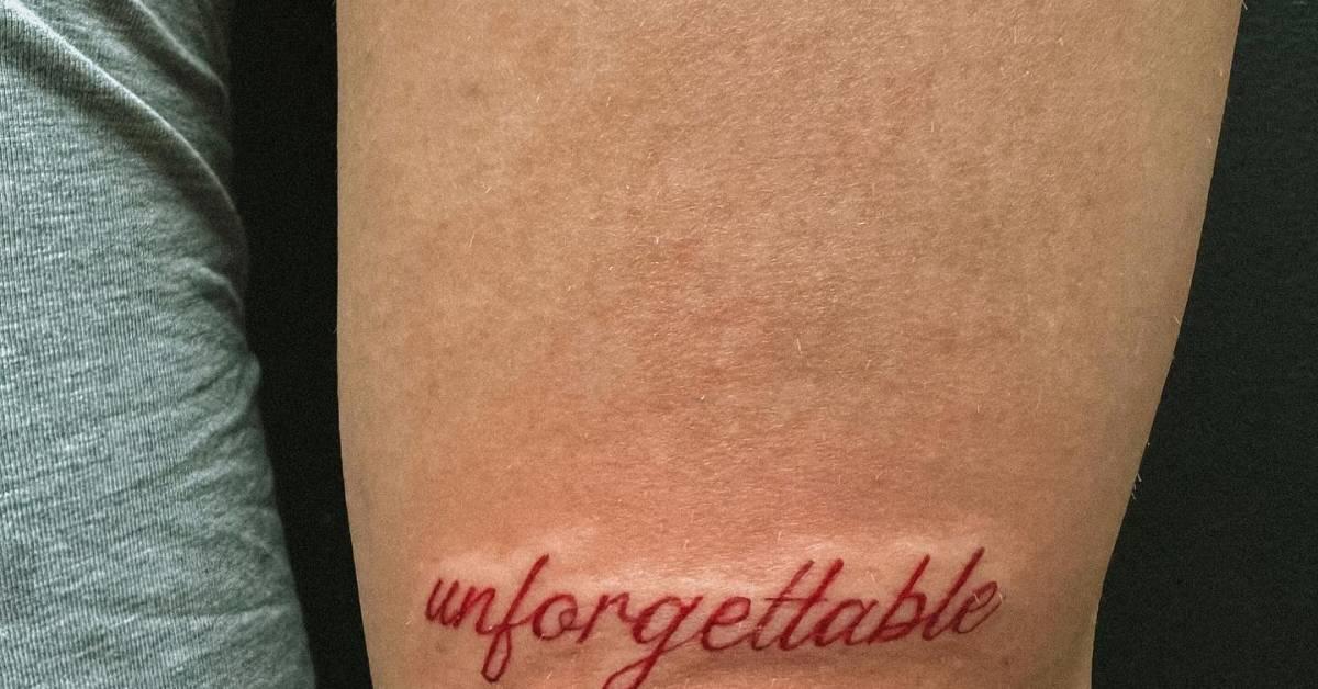 Word "unforgettable" in red ink tattooed on the tricep.