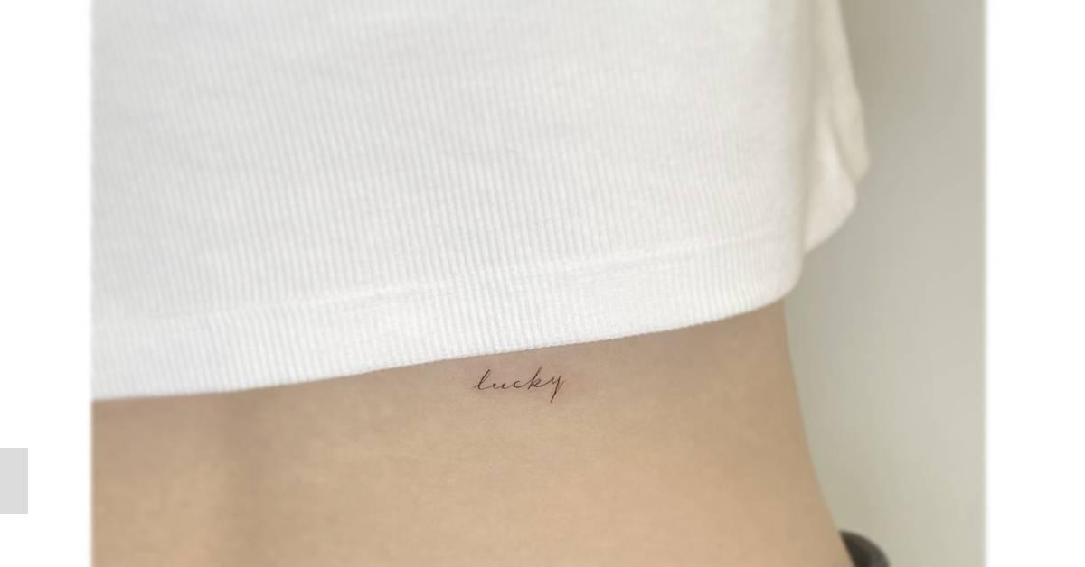 Handwritten word "lucky" lettering tattoo placed on the