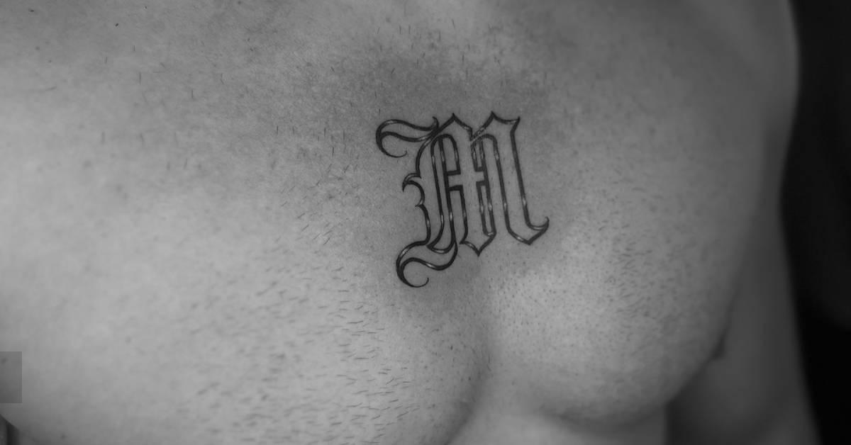 Letter "M" tattoo in gothic font located on the chest.