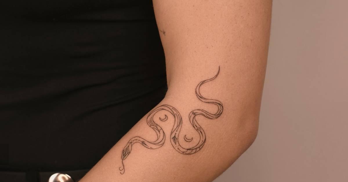 Fine line style snake tattoo hand poked on the elbow.