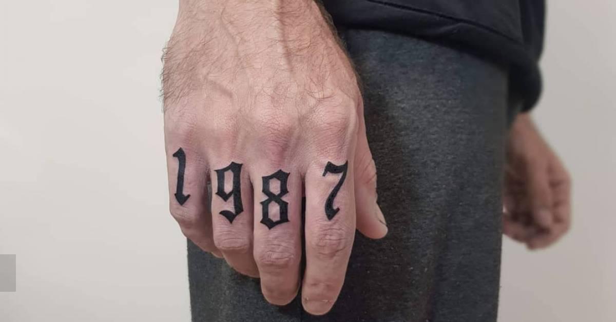 "1987" lettering tattoo located on the knuckles.
