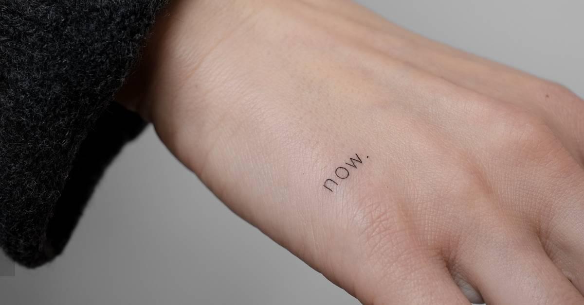 Little lettering tattoo of the word "now" located on