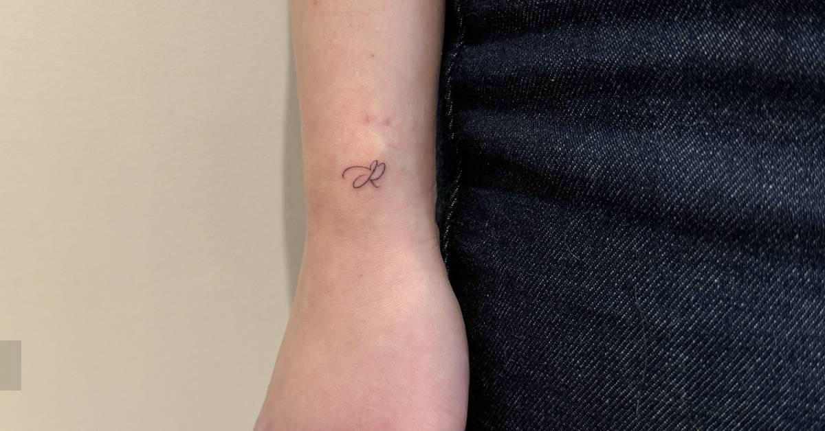 Tiny letter "R" tattoo in handwritten font located on