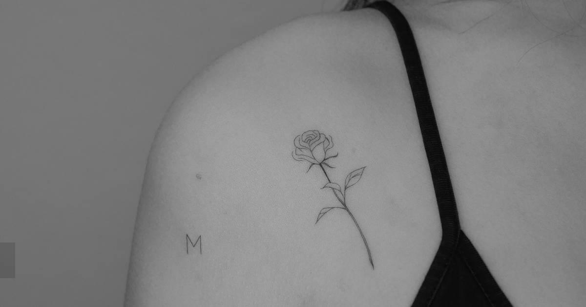 Fine line style letter "M" and rose tattoos located on