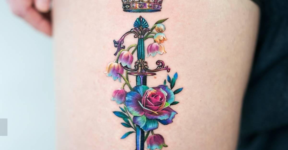 Realistic style sword, crown and flowers tattooed on