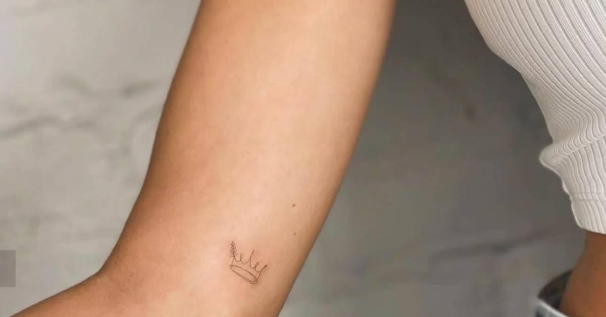 Fine line style crown tattoo located on the inner arm.