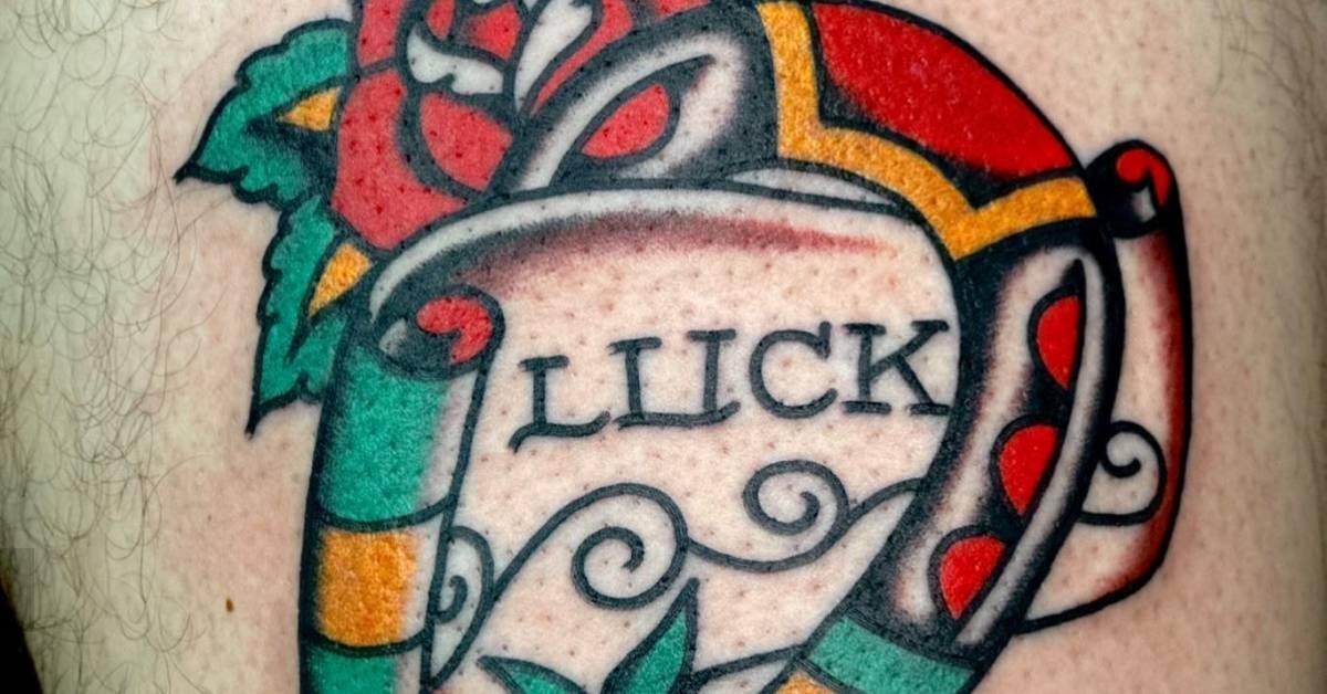 Horseshoe and word "luck" tattooed on the thigh,