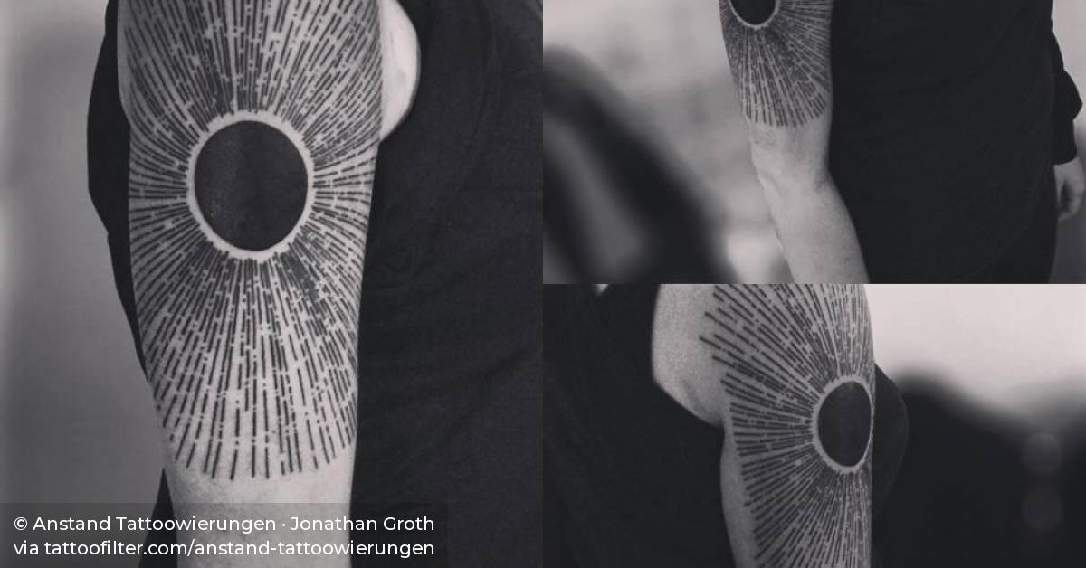 Blackwork style sun tattoo on the right upper arm.