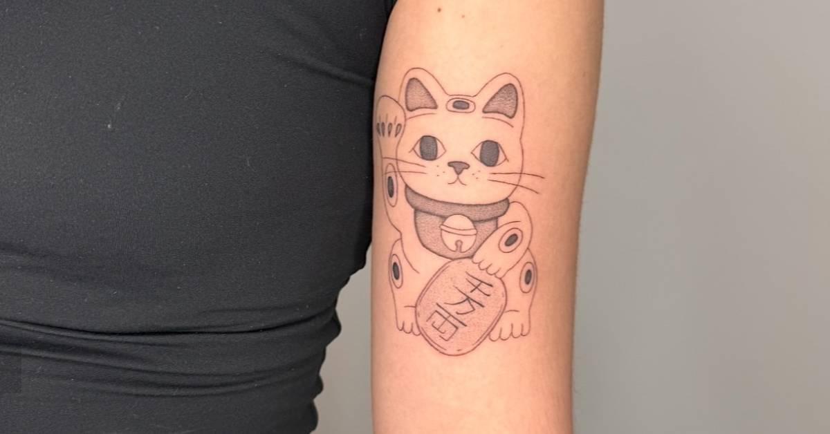 Single needle Maneki-Neko tattoo located on the bicep.