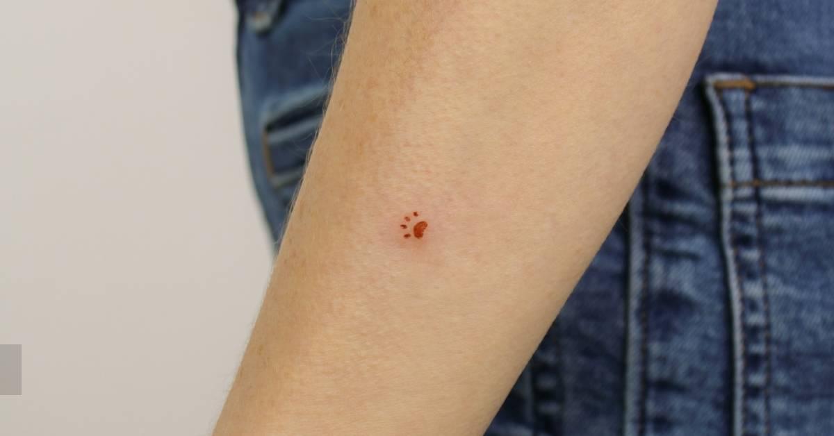 Micro dog paw print tattoo in red ink done on the