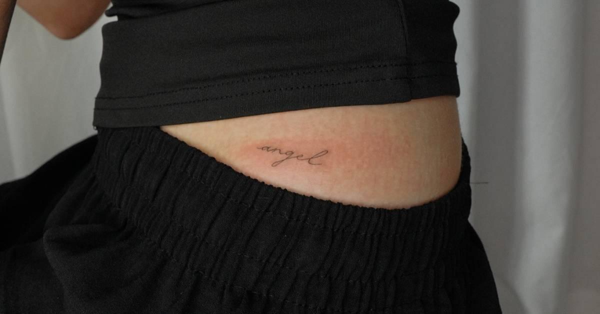 Lettering tattoo of the word "angel" placed on the hip.