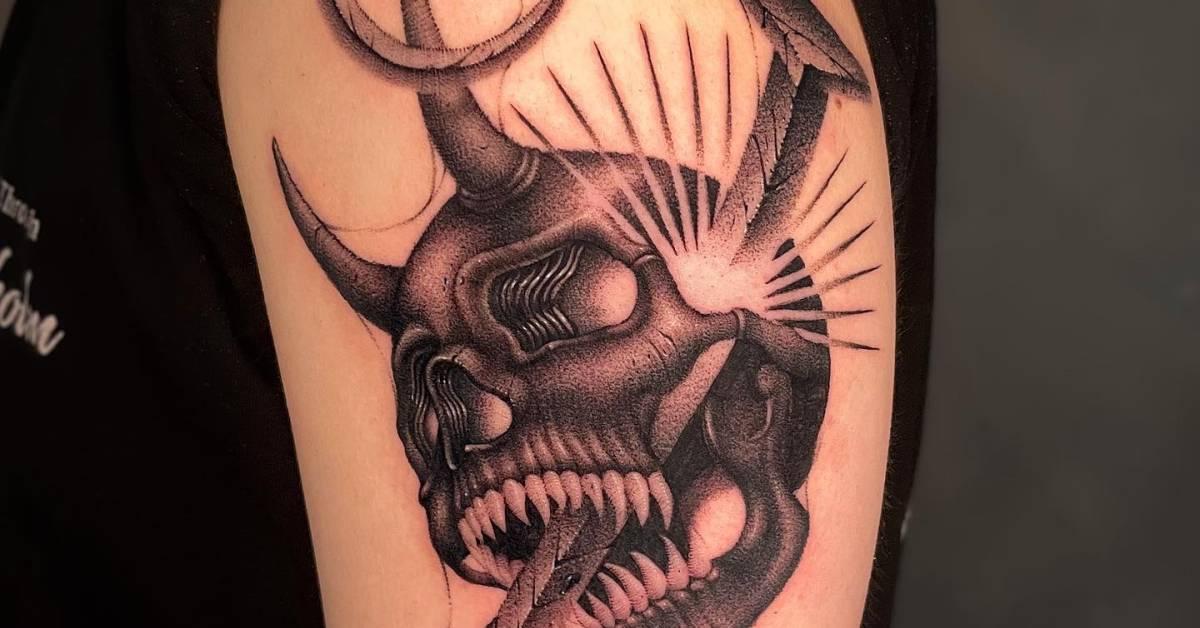 Devil skull and nail tattoo located on the upper arm.