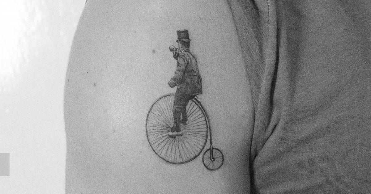 Micro-realistic penny-farthing tattoo on the shoulder.