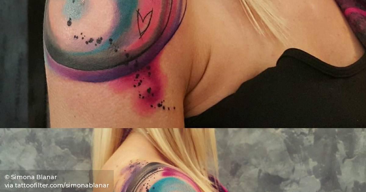 Watercolor/abstract style tattoo on the right shoulder.